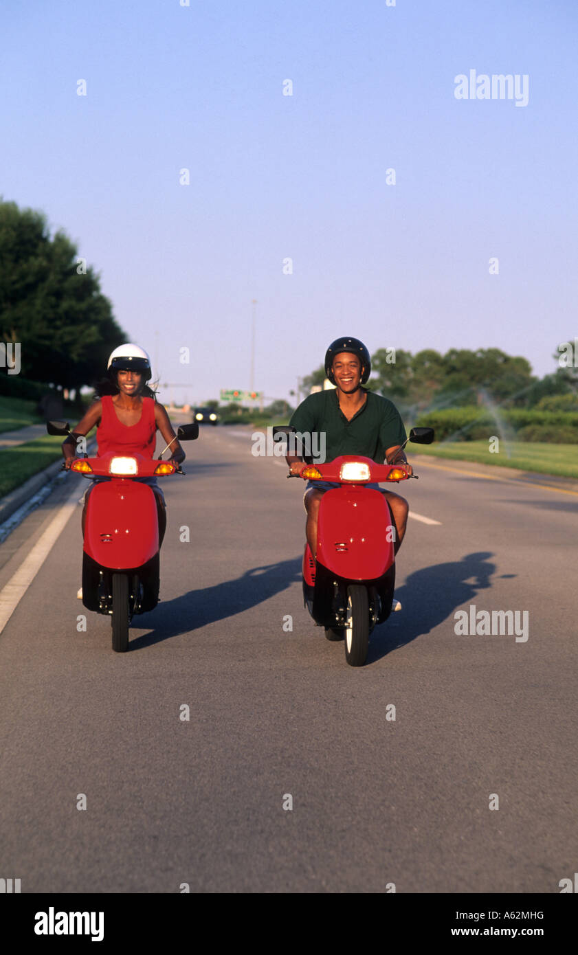 Happy black couple on red mopeds riding with helmets on road these ...