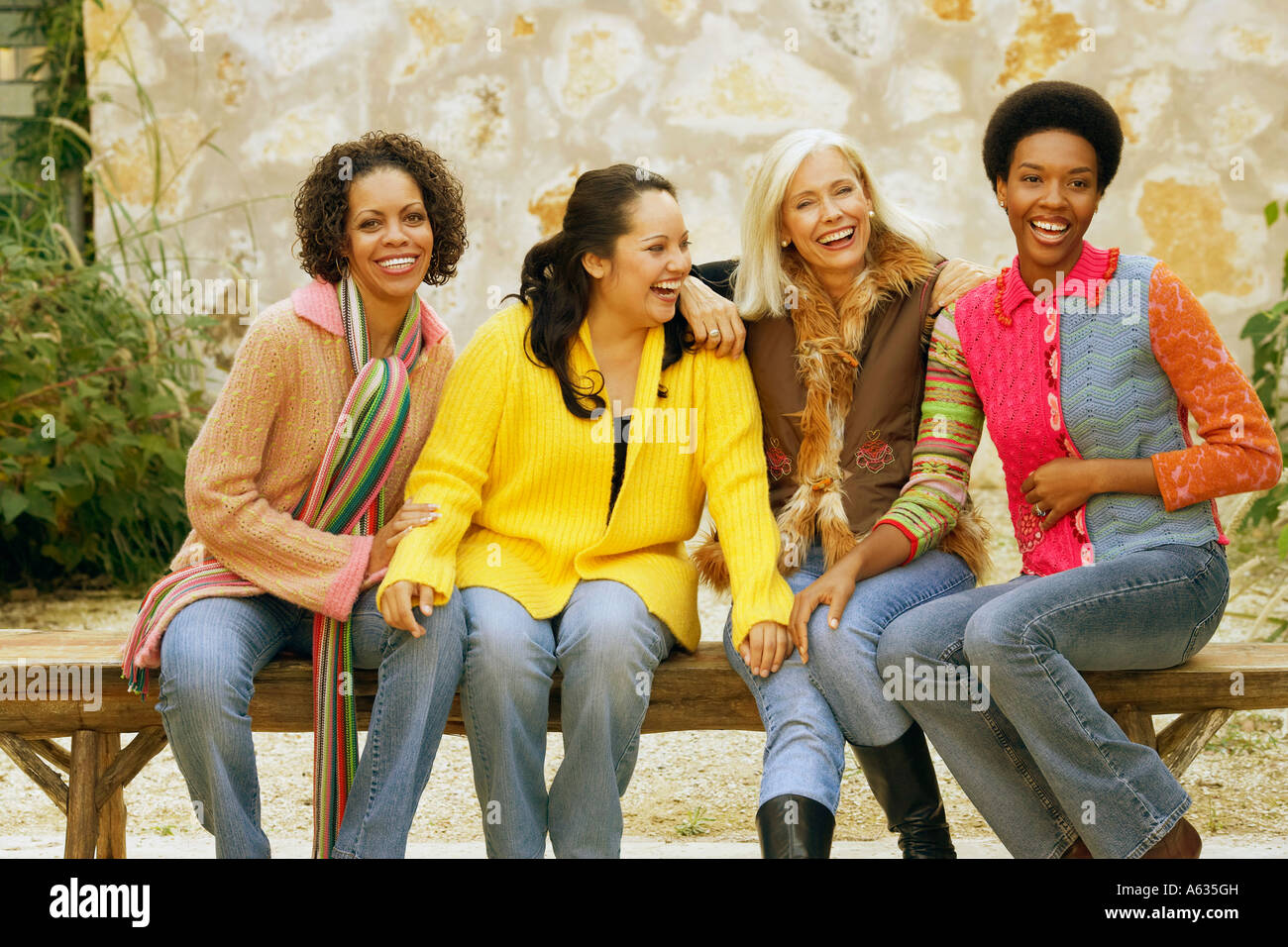 Four female friends sitting on a bench and smiling Stock Photo - Alamy