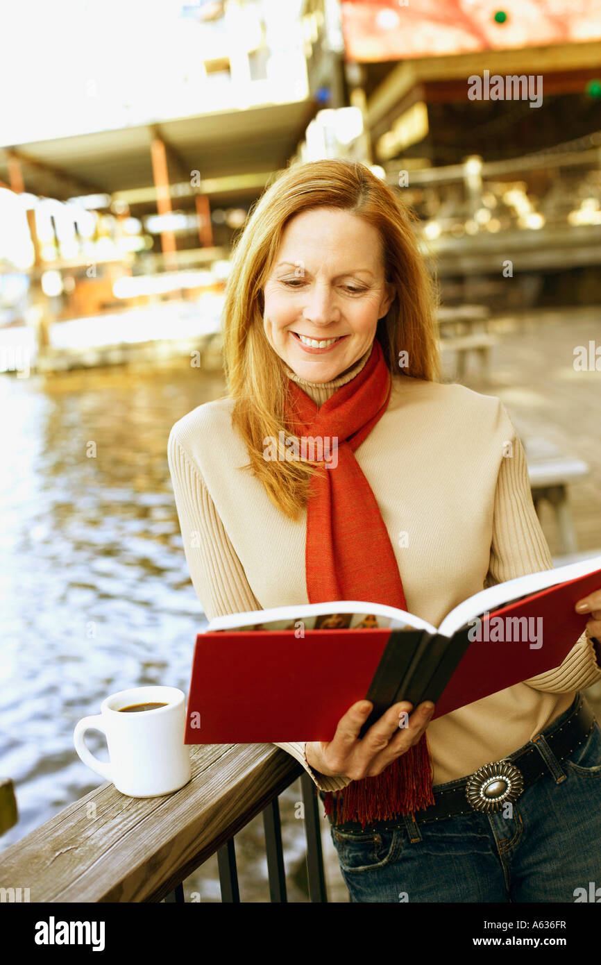 Young woman leaning against a railing and reading a book Stock Photo ...