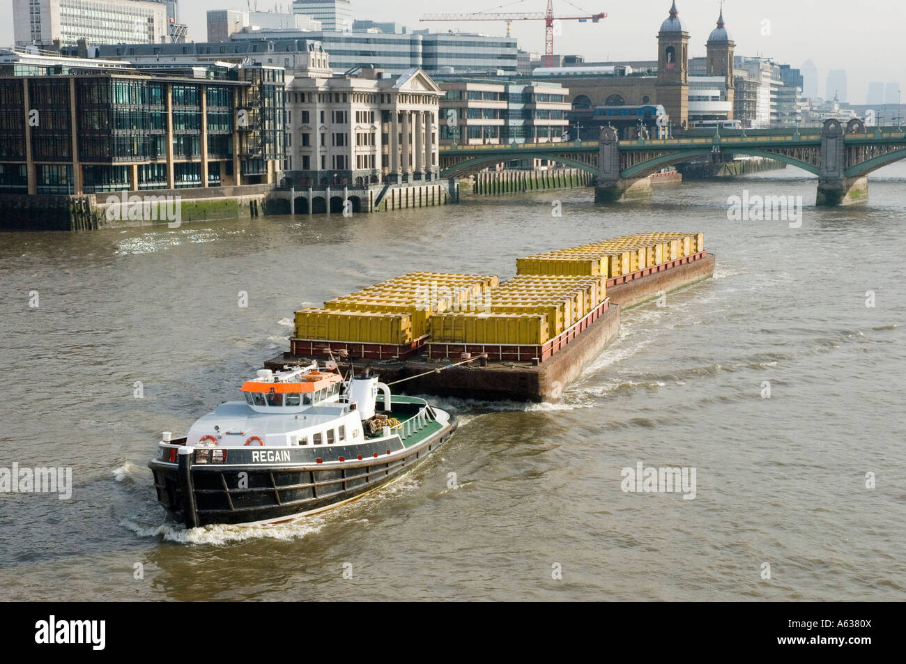 A tug pulling barges filled with cargo along the River Thames London ...