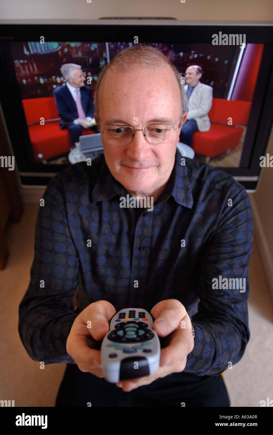 A MIDDLE AGED MAN WITH A REMOTE CONTROL WHILE A NEWS PROGRAMME APPEARS ...
