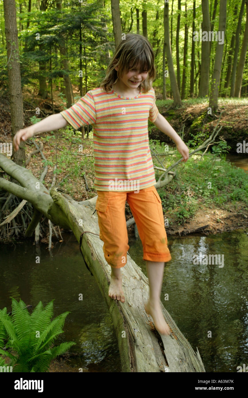 young girl walking over a tree which has fallen across a stream in a ...