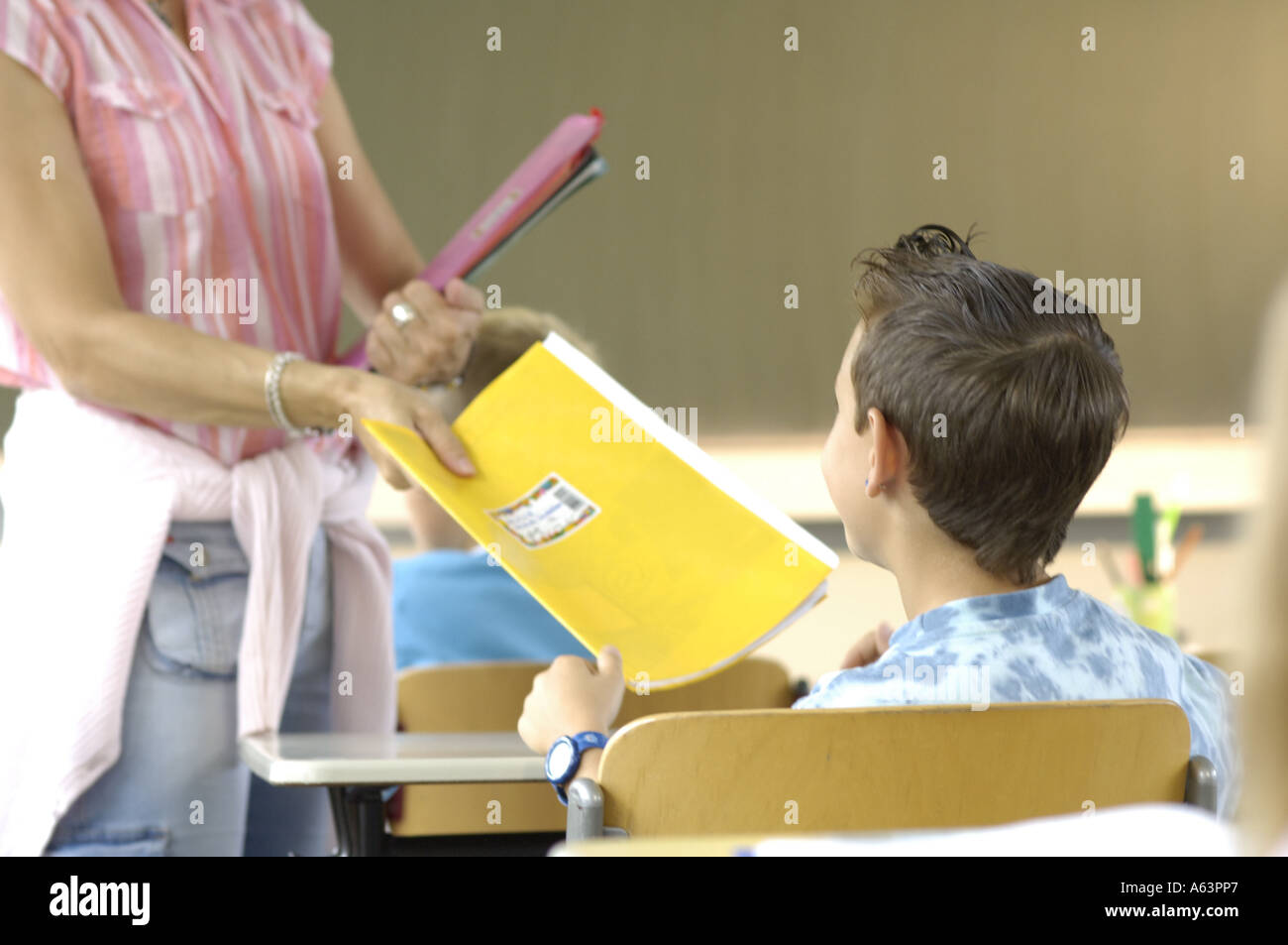 Teacher giving exercise book to boy in classroom Stock Photo - Alamy