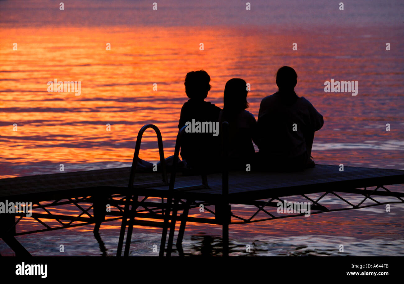 Friends enjoy the sunset while sitting on a dock on a Minnesota lake ...