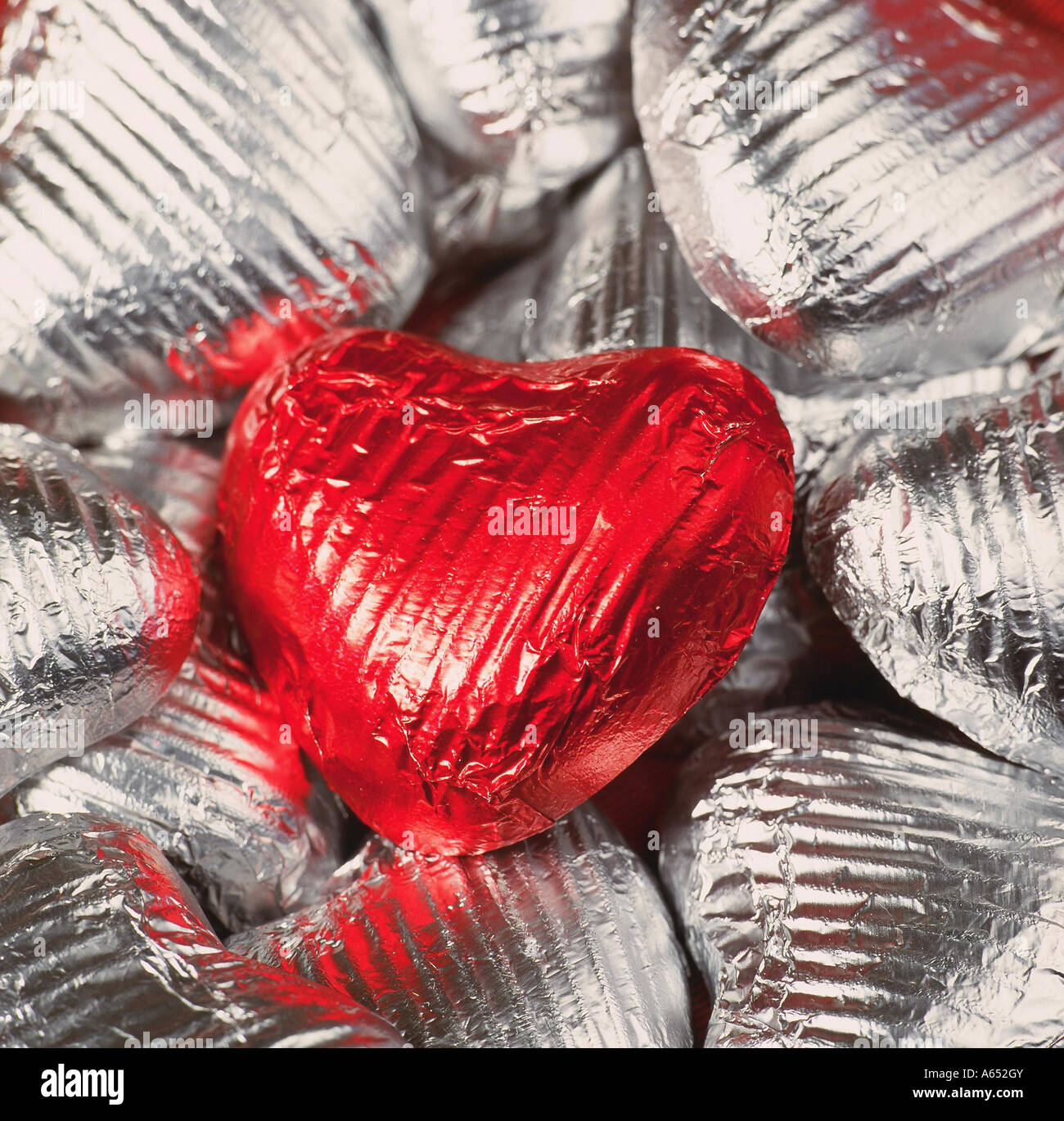 A single wrapped chocolate heart in red foil on silver hearts Stock ...