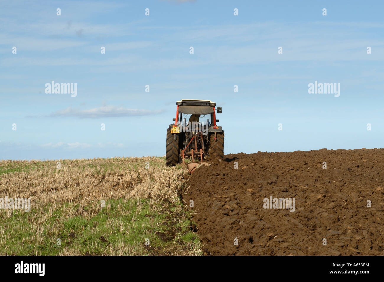 Farmer driving tractor and ploughing a grassy field against a blue sky ...