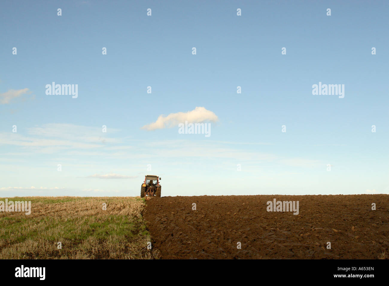 Farmer driving tractor and ploughing a grassy field against a blue sky ...