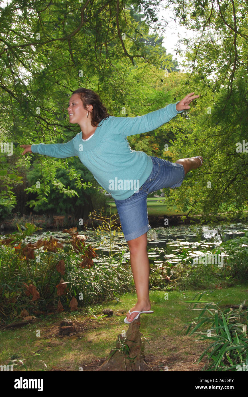 A teenage girl balancing on a tree stump in a "flying" pose, in the ...