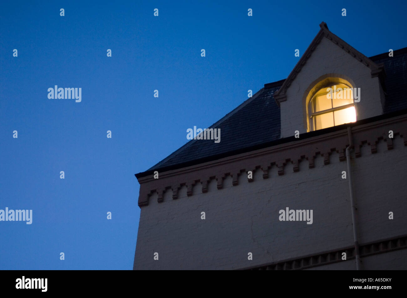 single Lighted window on top floor of building at night Stock Photo - Alamy