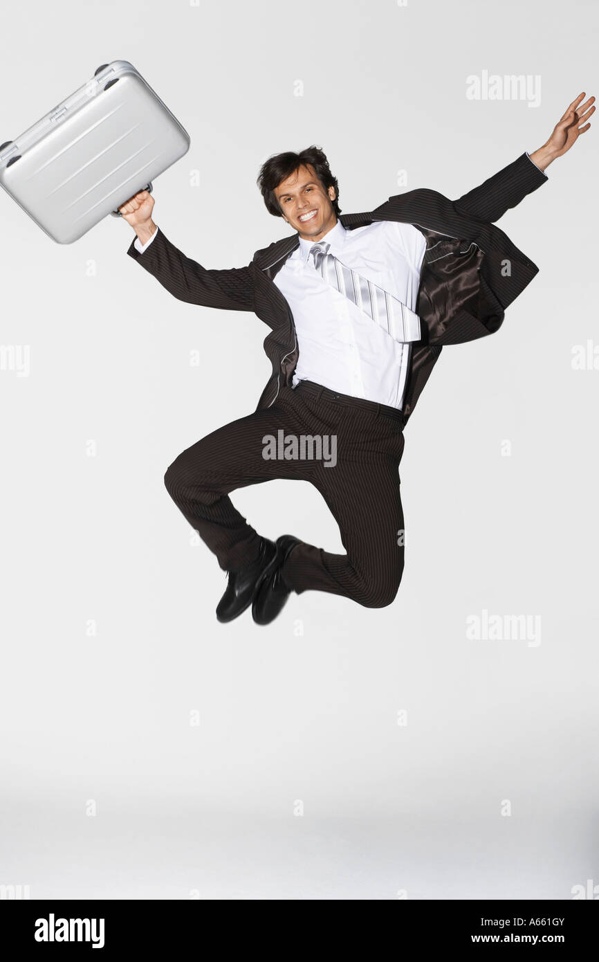 Smiling, young businessman holding briefcase jumping, clicking heels ...