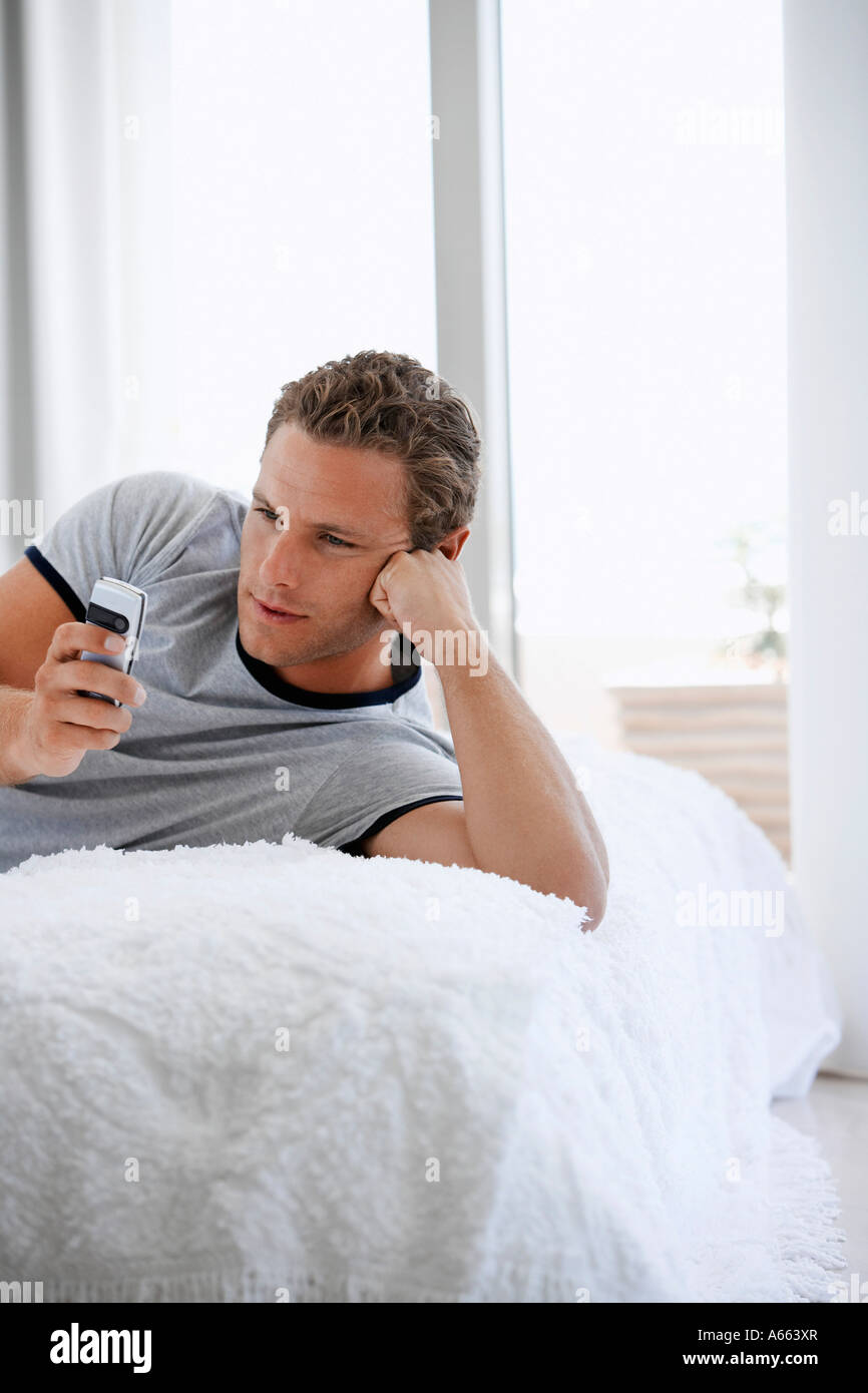 Young man lying on bed using mobile phone, portrait Stock Photo - Alamy