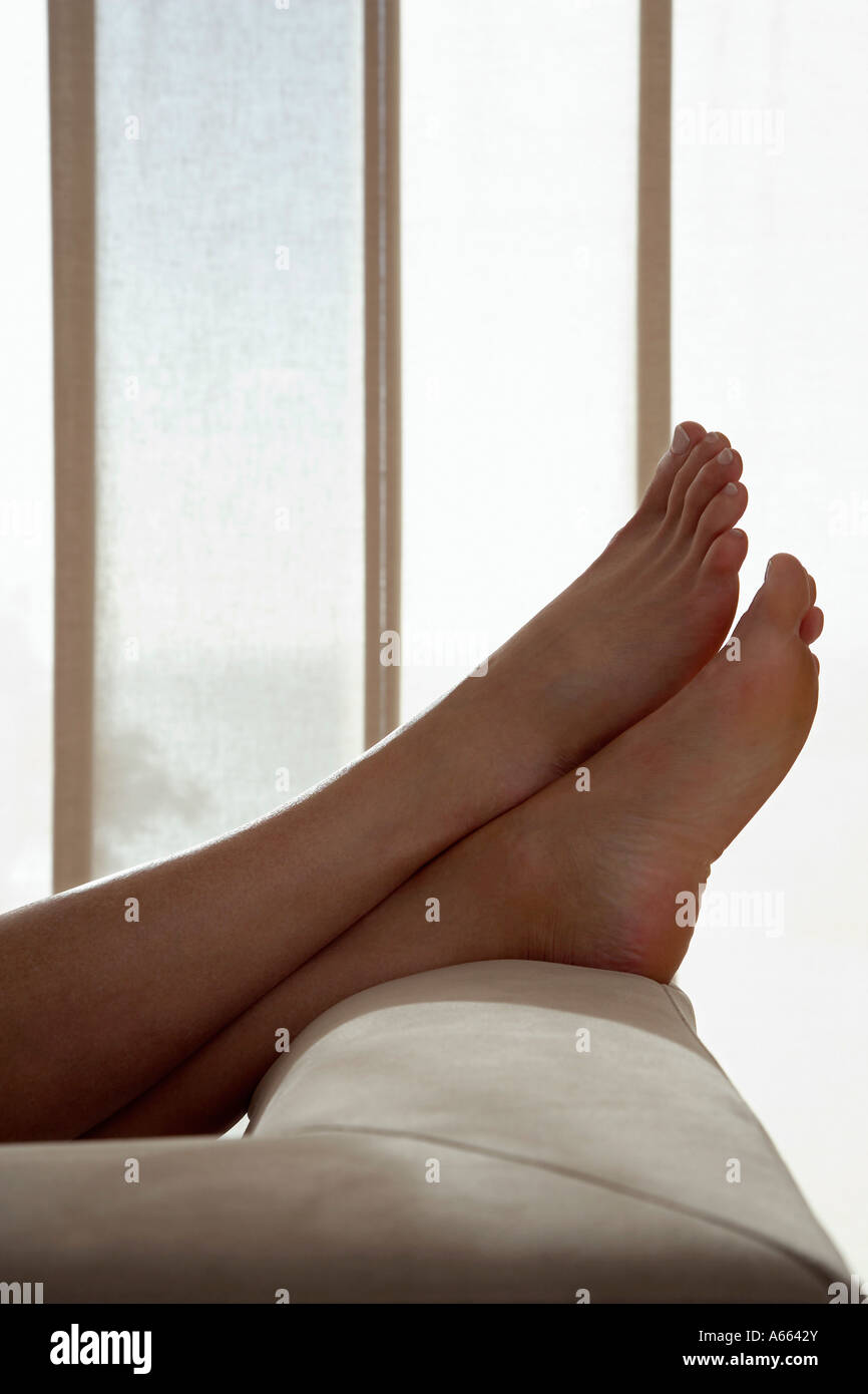 Woman resting with feet up on sofa in living room, close up of feet ...
