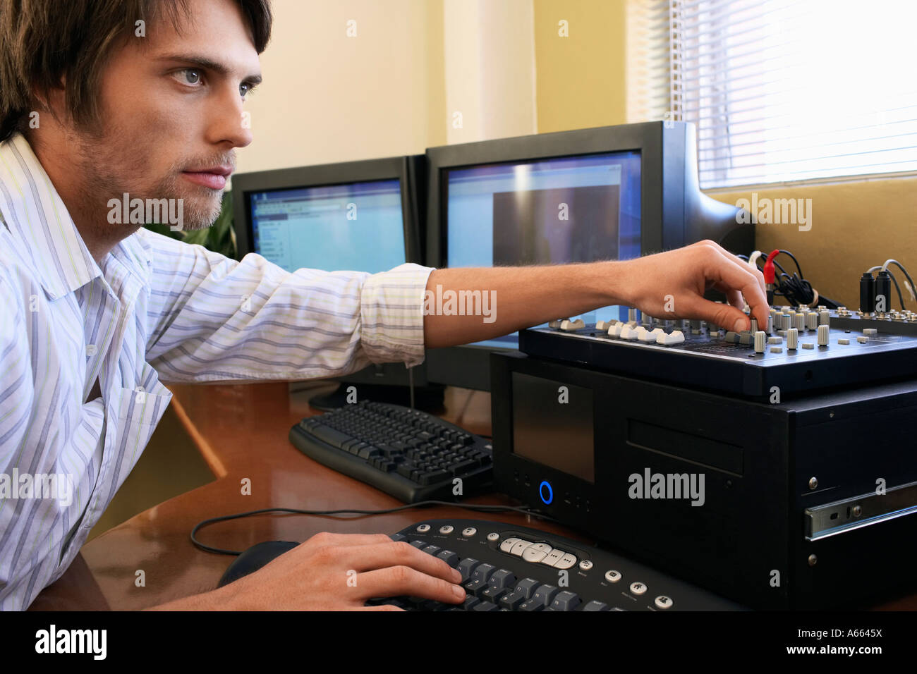 Man using computer keyboard and adjusting knob on mixer Stock Photo - Alamy