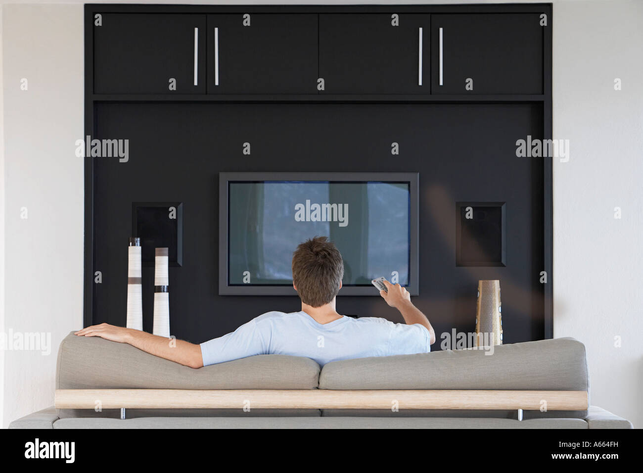 Man using remote control, sitting in front of flat screen television ...