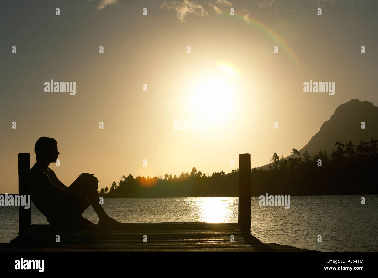 Man sitting on dock by lake, side view Stock Photo - Alamy