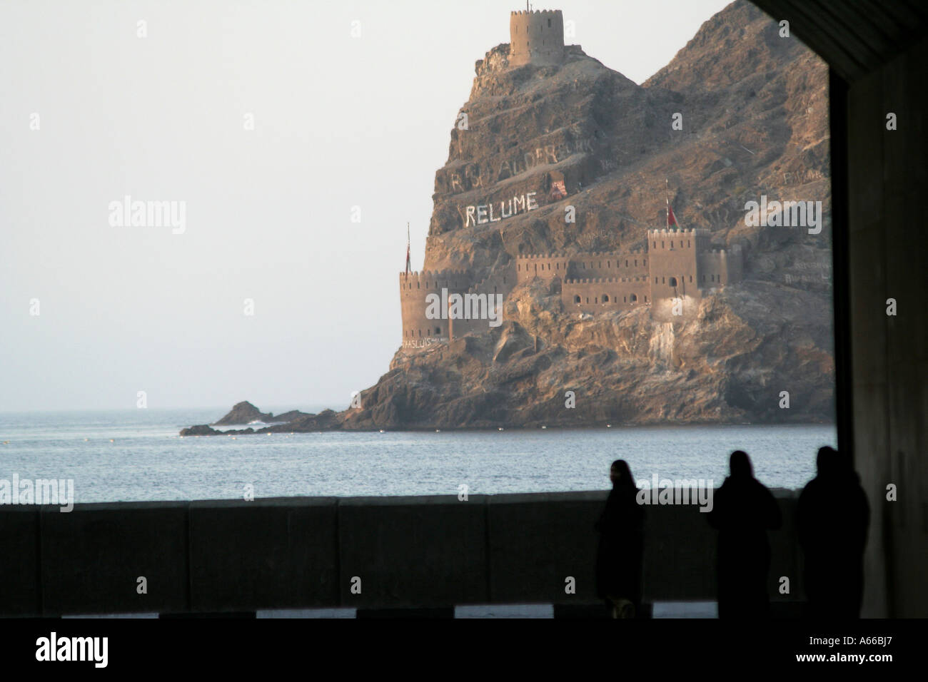 View through a tunnel of Omani women and a cliffside watchtower, Muscat ...