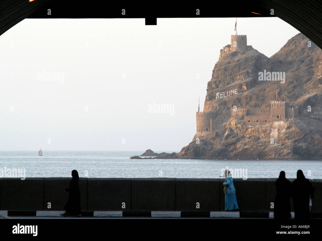 View through a tunnel of Omani women and a cliffside watchtower, Muscat ...