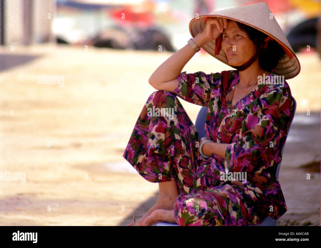 A Vietnamese woman wearing a typical hat sits under the shade in the ...
