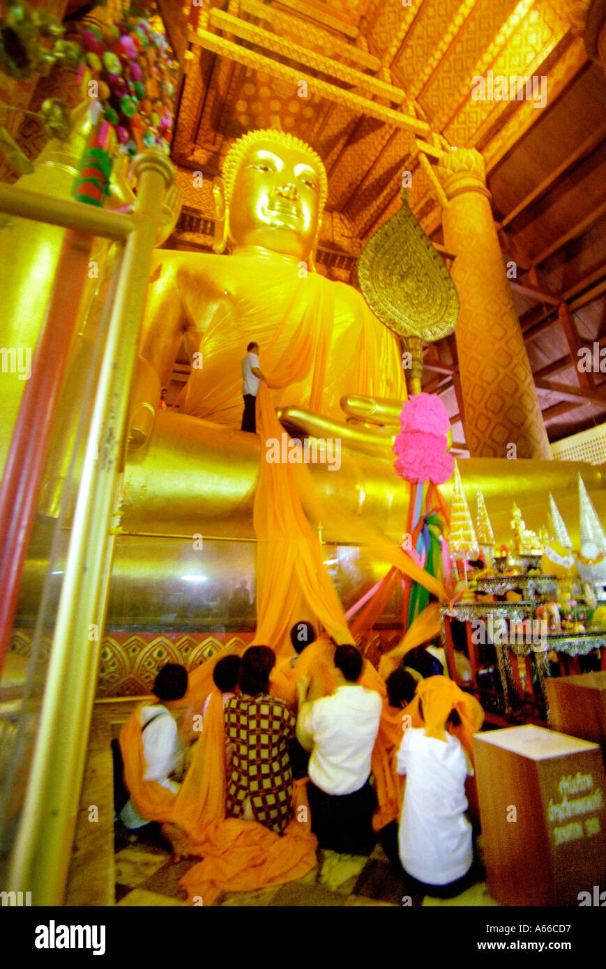 A large Buddha is being dressed with a yellow cloth by his faithful at ...