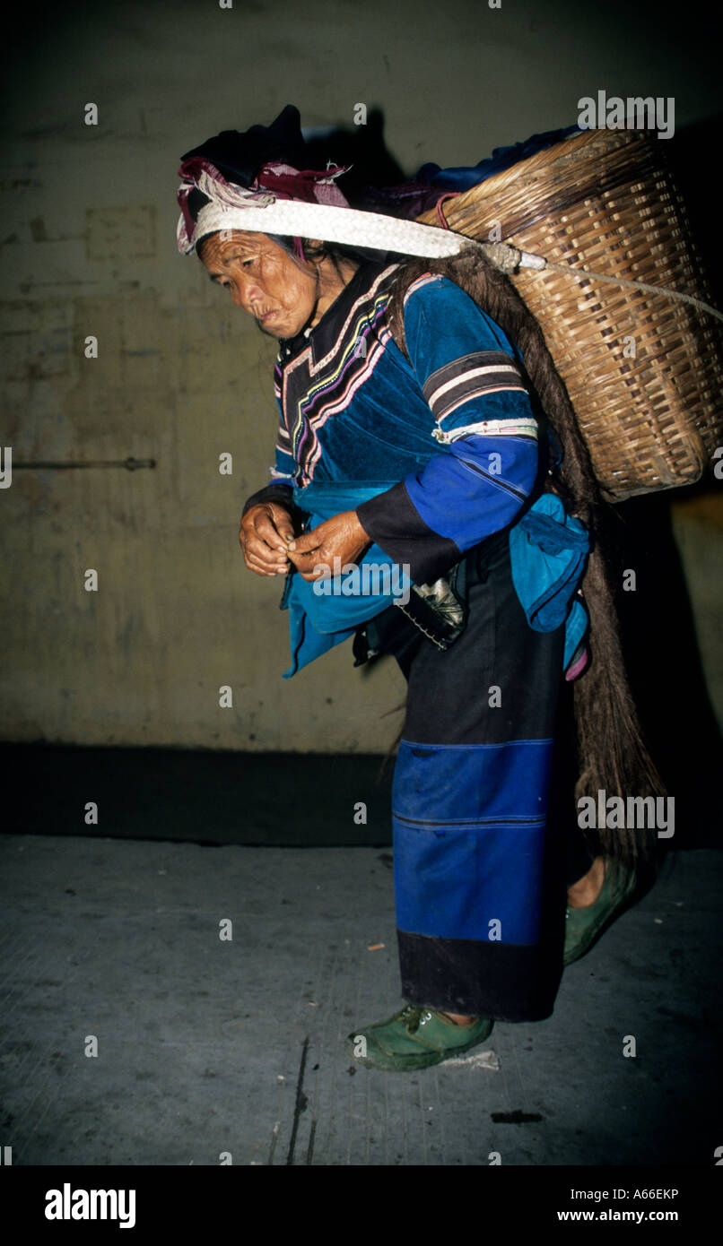 Woman of Yi ethnic minority in traditional dress carrying a basket with ...