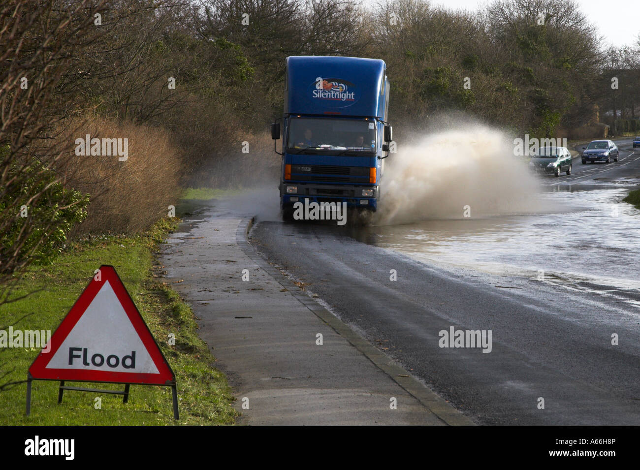 Large lorry driving (cars vehicles behind) splashing through flood ...