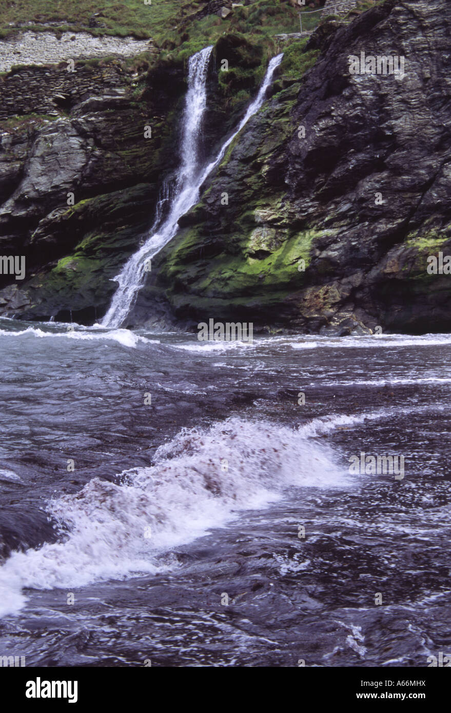 Tintagel waterfall flows down the cliff into the dark sea and breaking ...