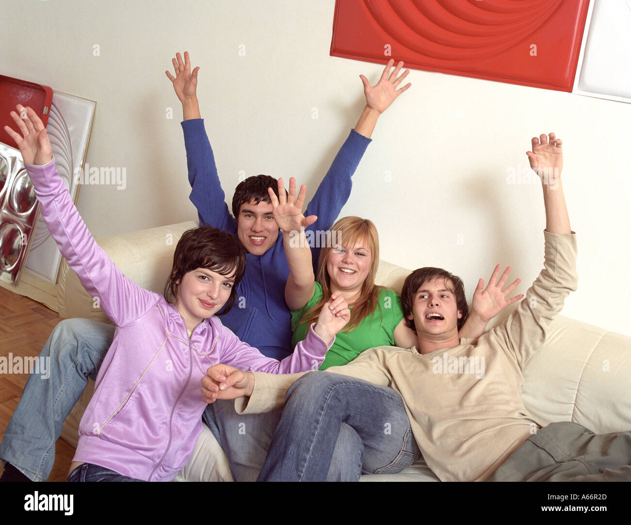 portrait of teenage friends on a sofa raising their arms in the air for ...