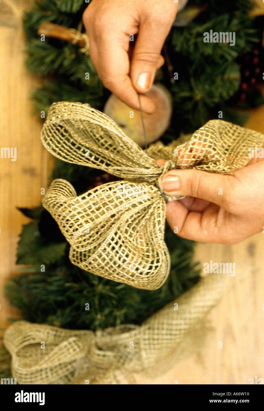 Close-up of hands attaching gold metallic ribbon bow to conifer garland ...