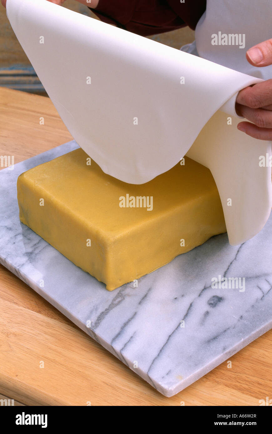 Close-up of hands laying white icing sheet on square cake covered with ...