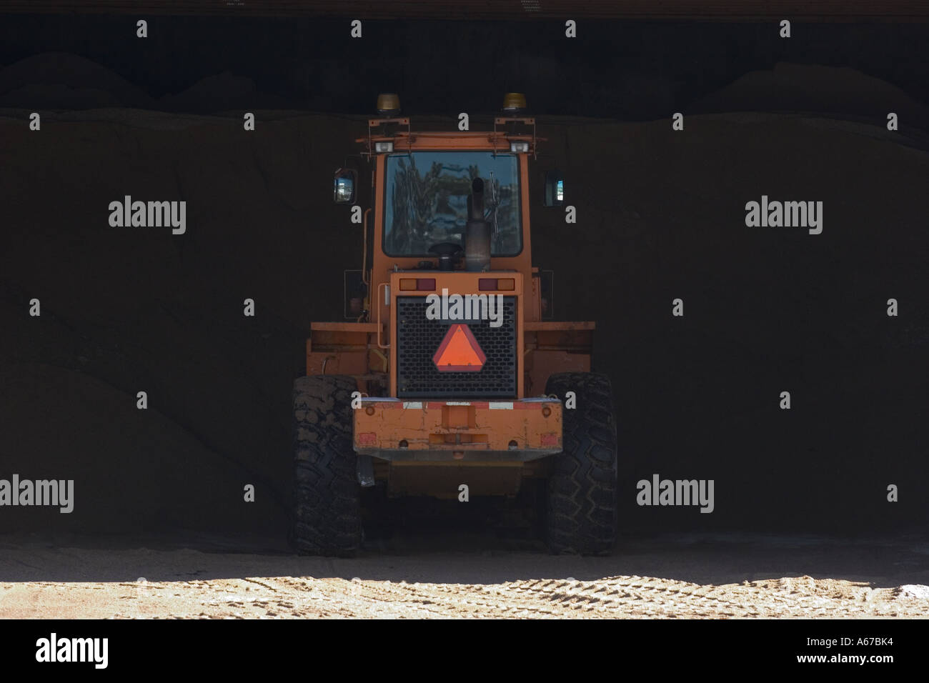 Front end loader parked in building with mounds of dirt in background ...