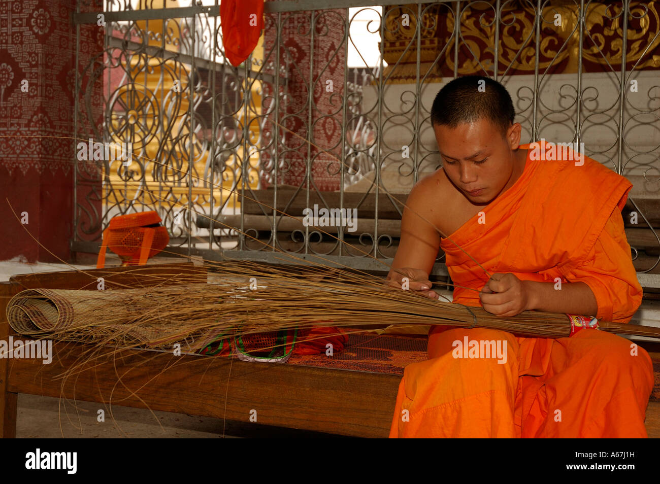 A young novice Buddhist monk repairs a straw broom at the Wat Saen ...