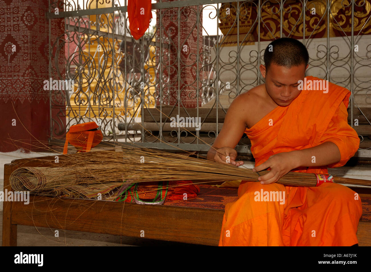 A young novice Buddhist monk repairs a straw broom at the Wat Saen ...