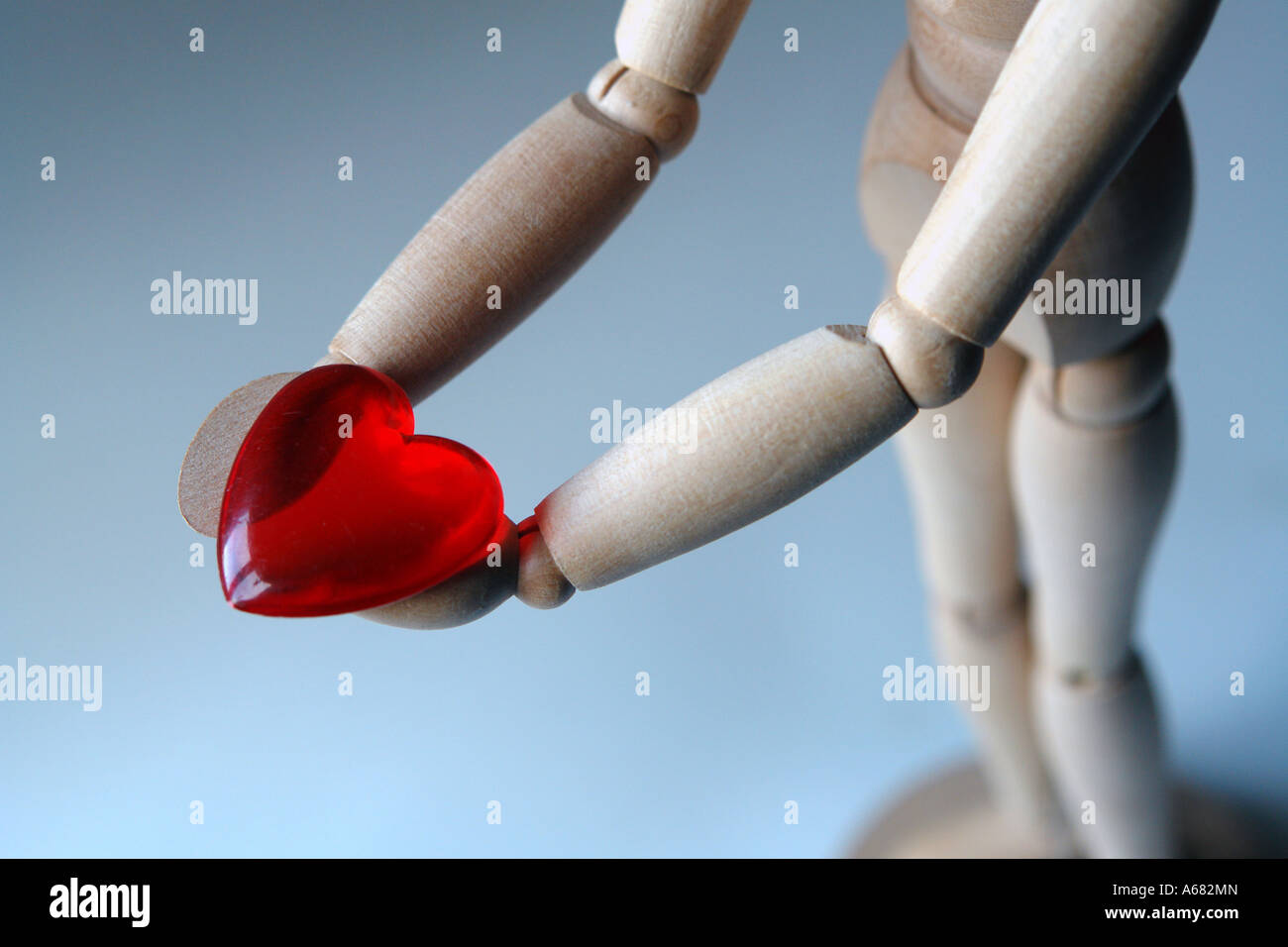 Wooden figure stretching out its arms with a red heart in its hands ...