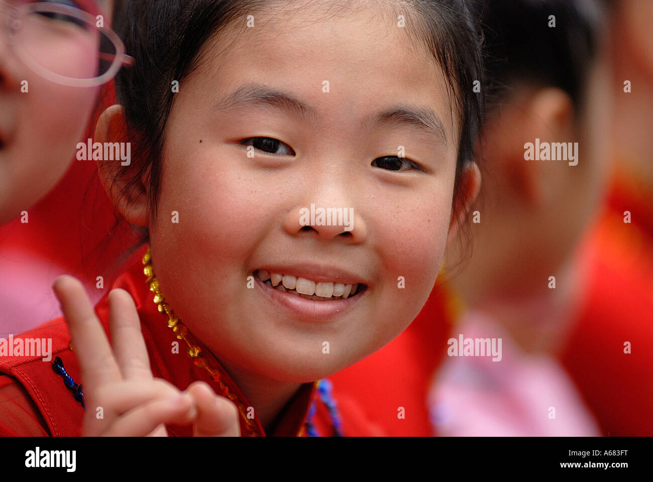 A young Chinese girl happily smiles as she makes the victory sign ...