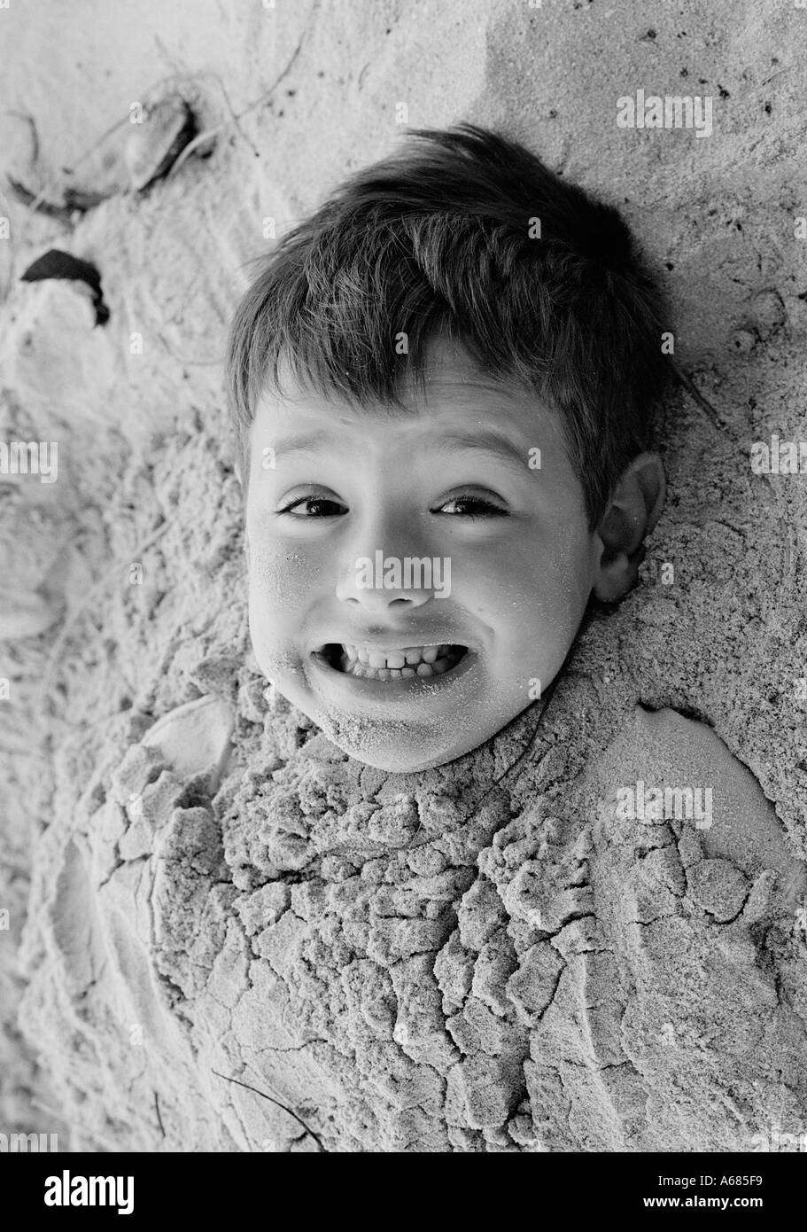 boys head poking out of the sand looking up to camera pulling a funny ...