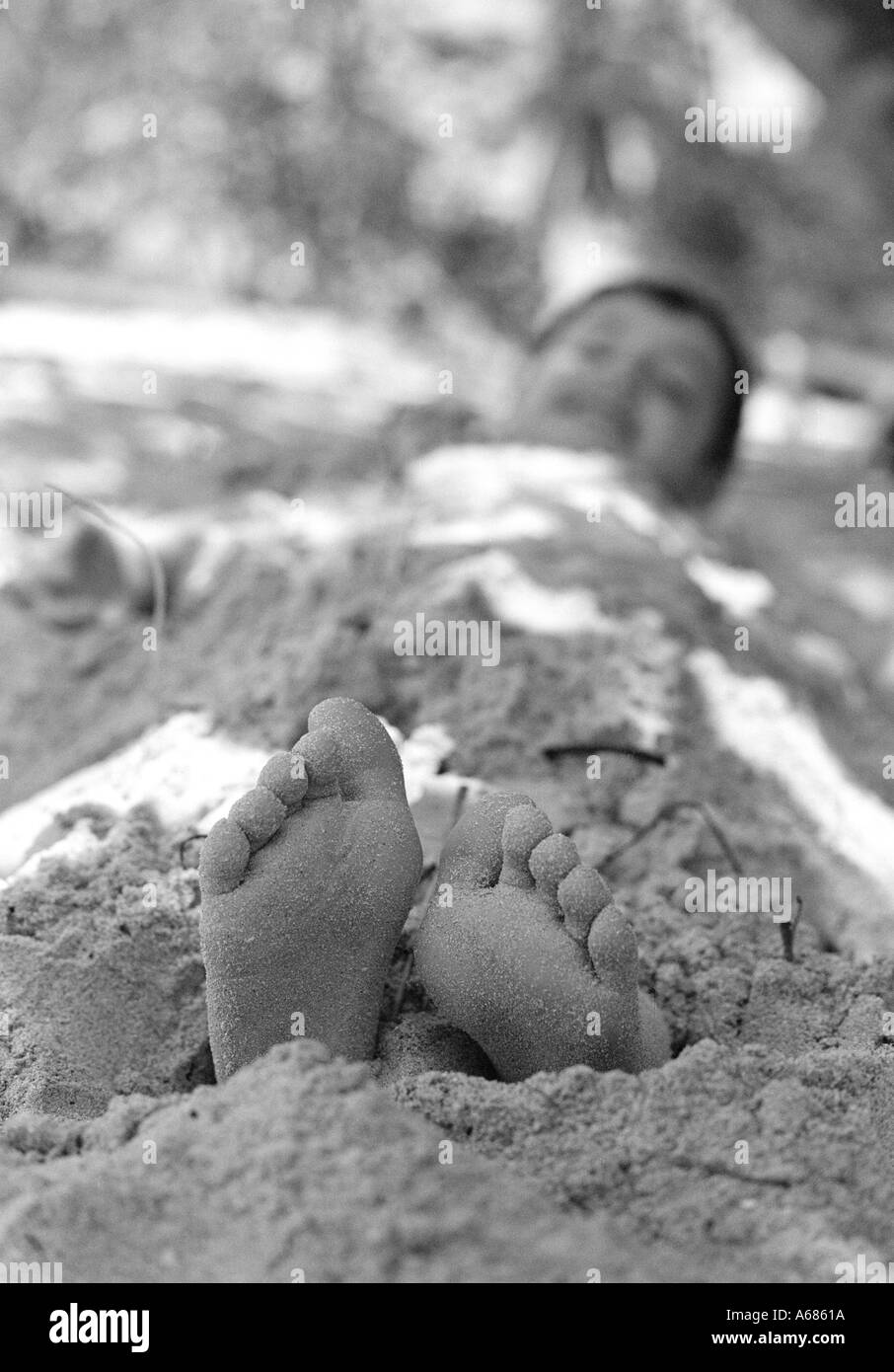 boy buried in sand with just his feet and head sticking out in dappled ...