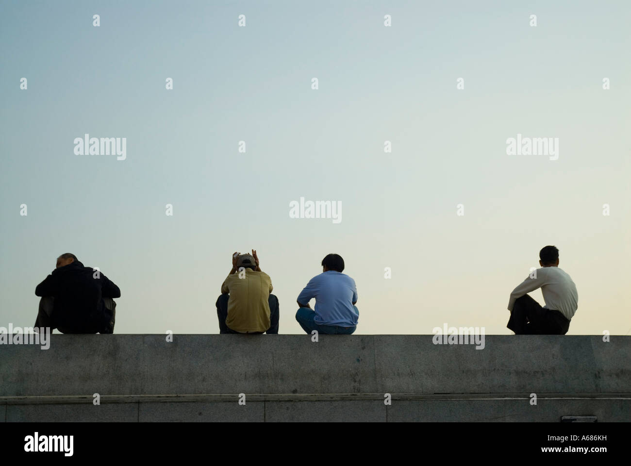Young men sit and watch the sun set over the water on the island of ...