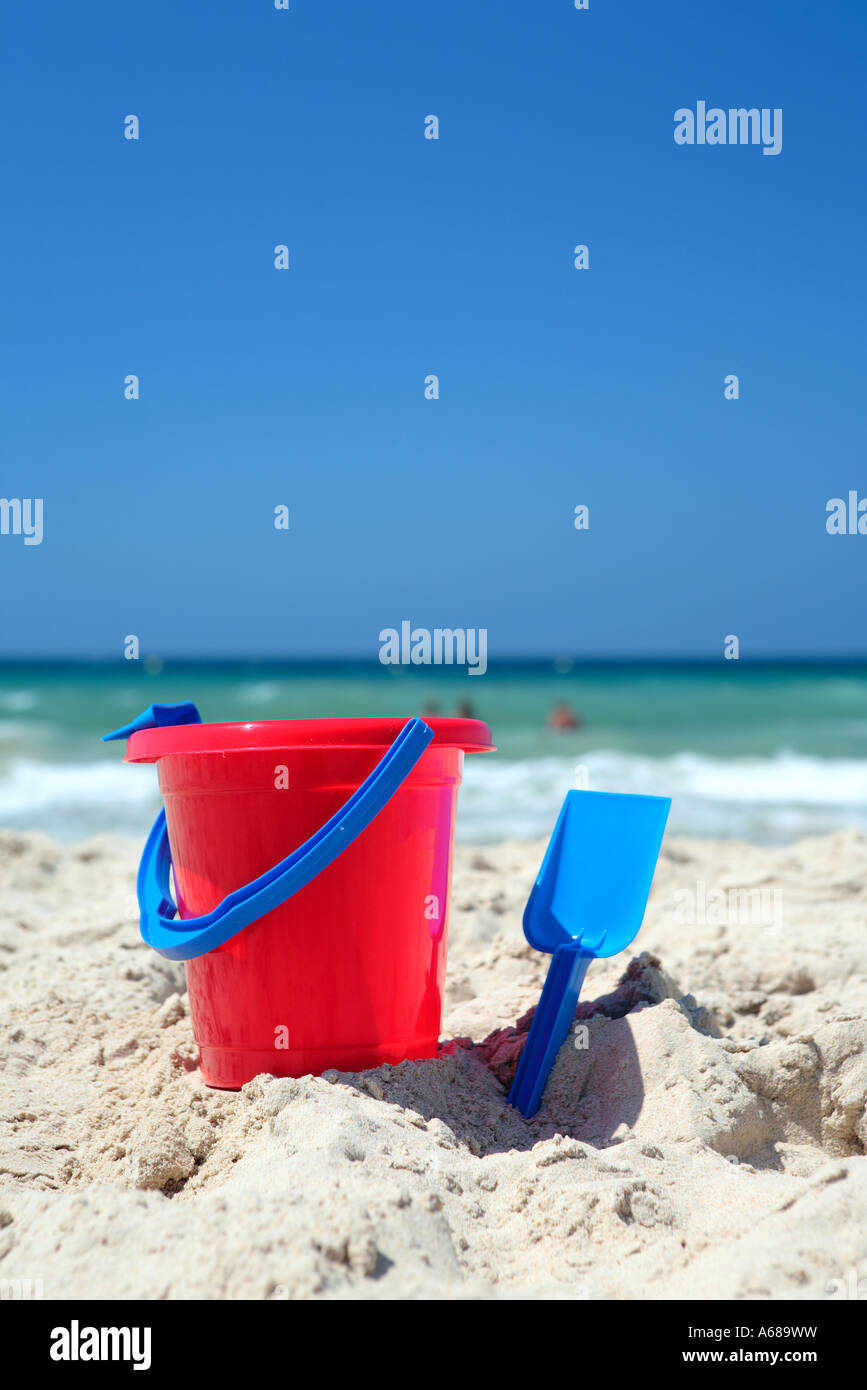 Red bucket and blue spade on sunny sandy beach on vacation or holiday ...