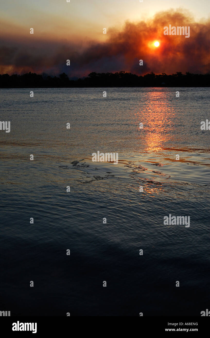 Sun setting behind smoke from bushfire, reflected in river Stock Photo ...