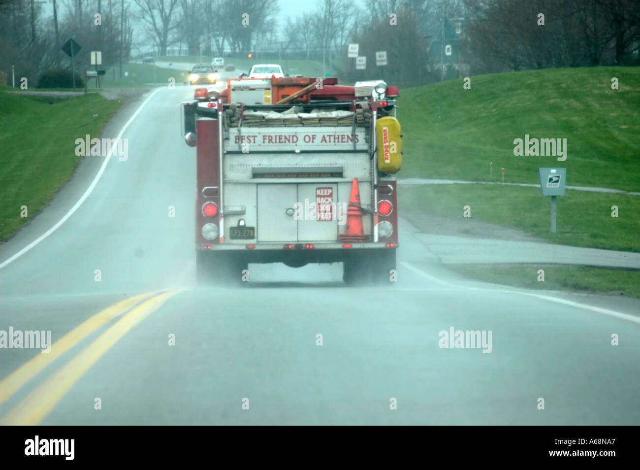 Rear view of a red fire truck speeding down a rain slicked road in the ...
