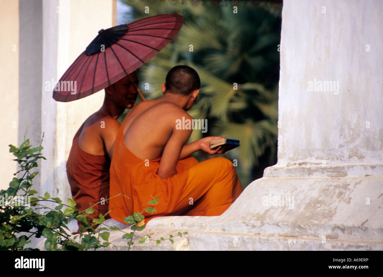 Two buddhist monks sitting on a wall of a temple in Luang Prabang.Laos ...
