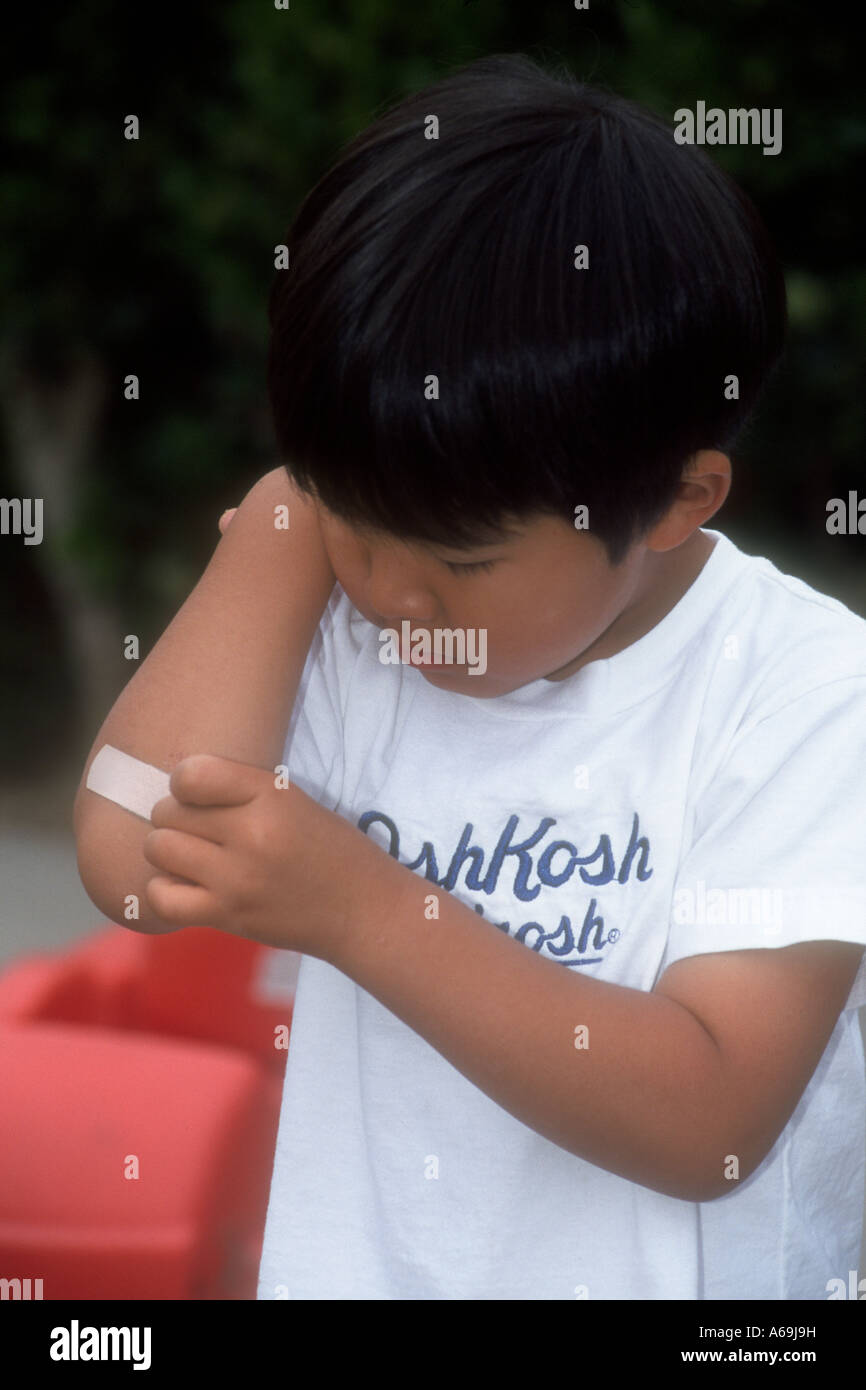 Asian preschooler examines bandage on arm Stock Photo - Alamy