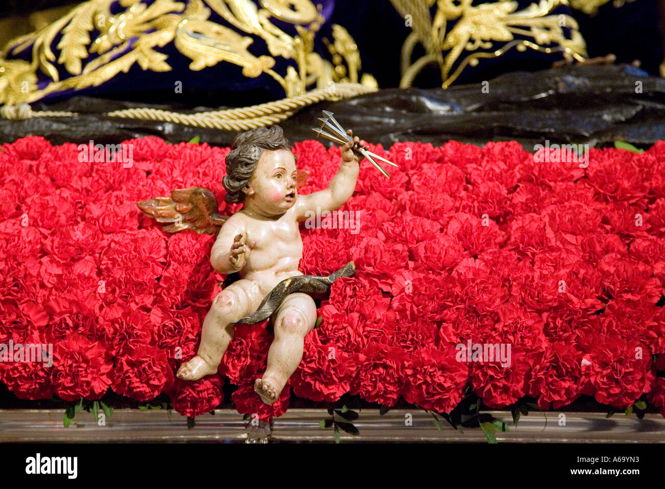 Figure of a cherub with arrows on a red carnations background ...