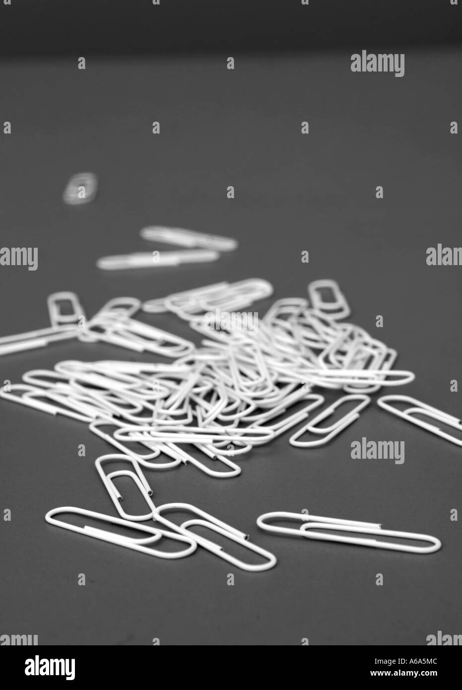 white paper clips scattered on a grey background black and white image ...