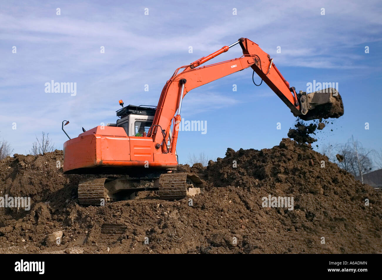 Construction digger on a mound of earth bucket tipping Stock Photo - Alamy