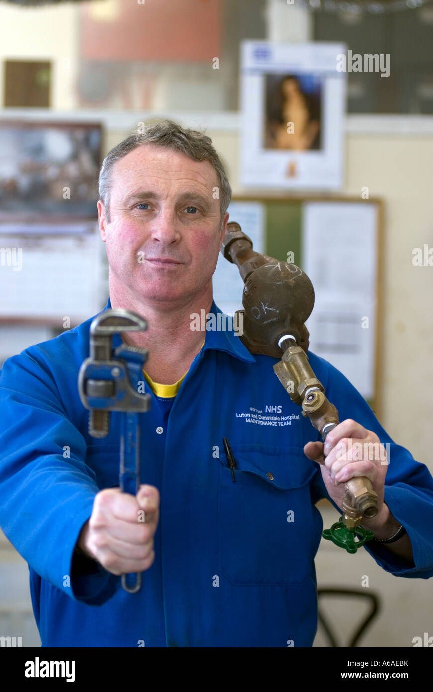 Maintenance worker for the NHS holds a wrench and a piece of pipe in a ...