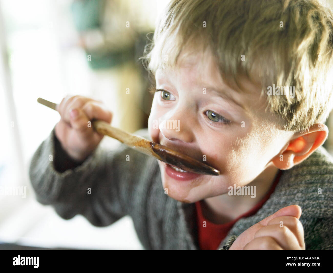young child with wooden spoon eating chocolate icing from the mixing ...