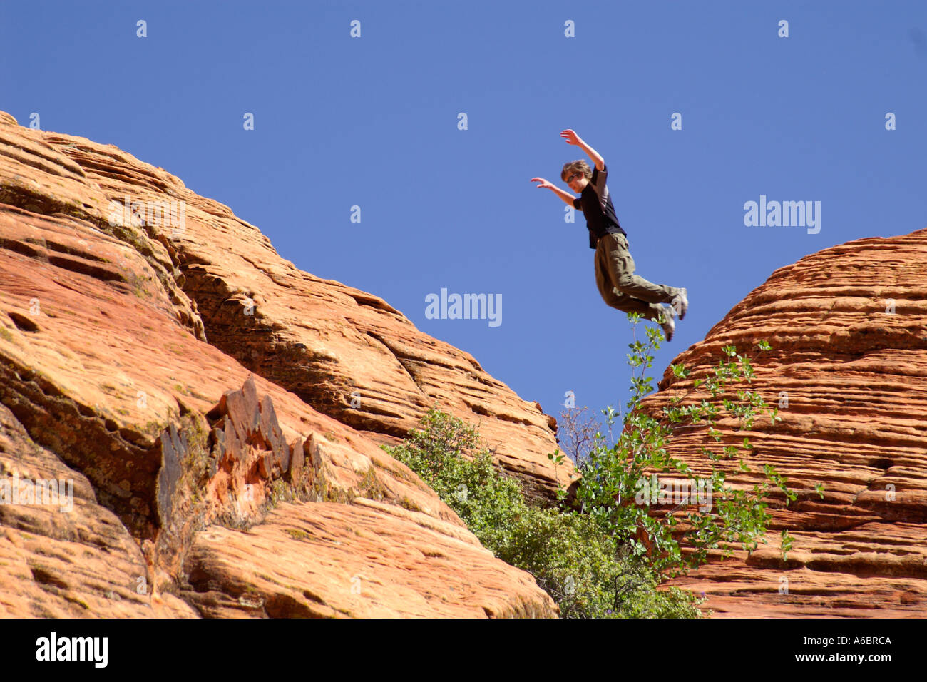 teenage boy jumping gap between rocks Snow Canyon State Park Utah U S A ...
