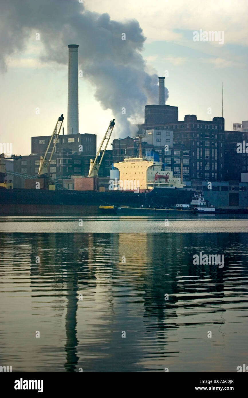 A container ship is docked in front of a factory with smoke or steam ...