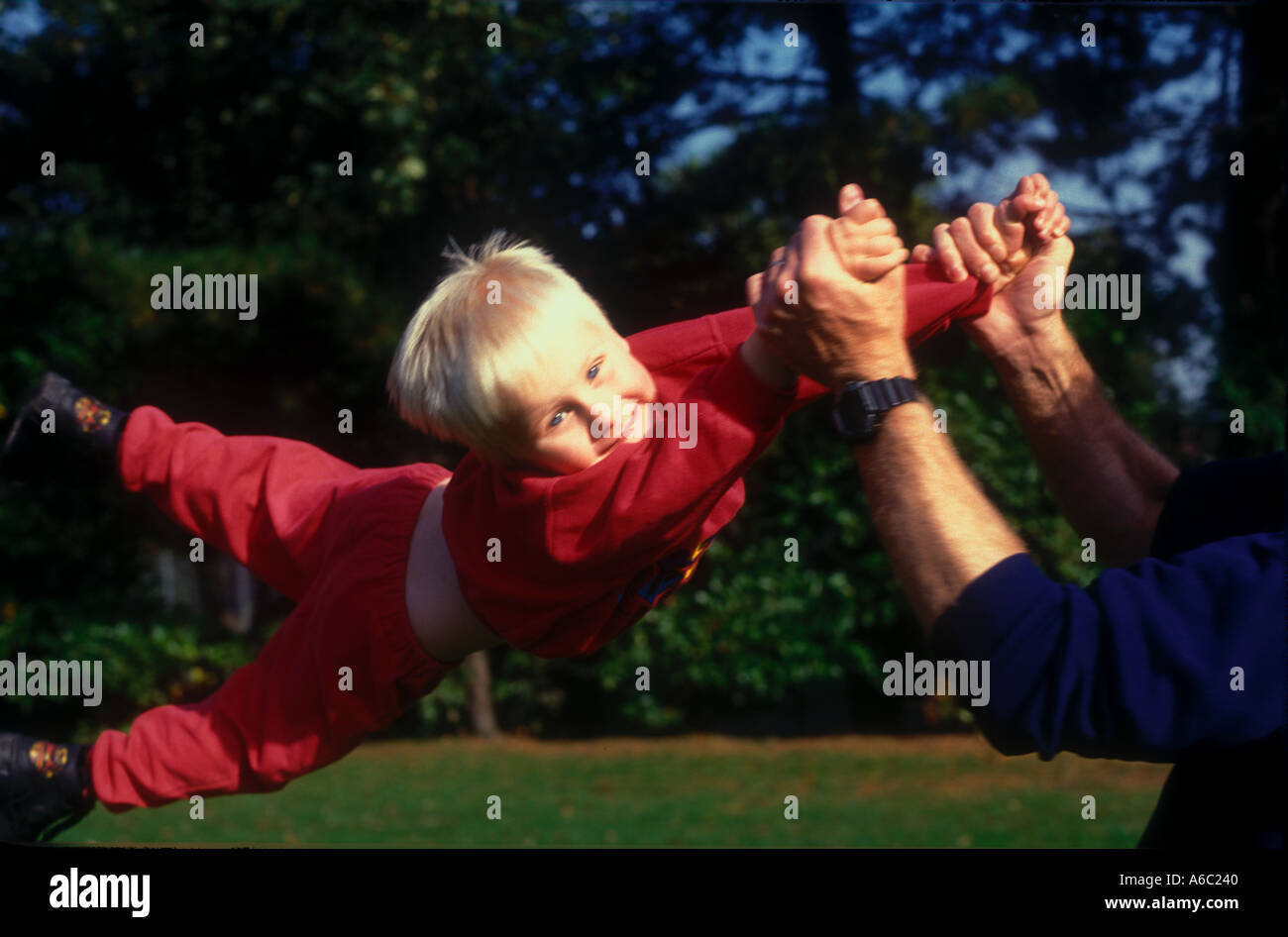 Young boy being spun around in the air by arms by father in the park ...